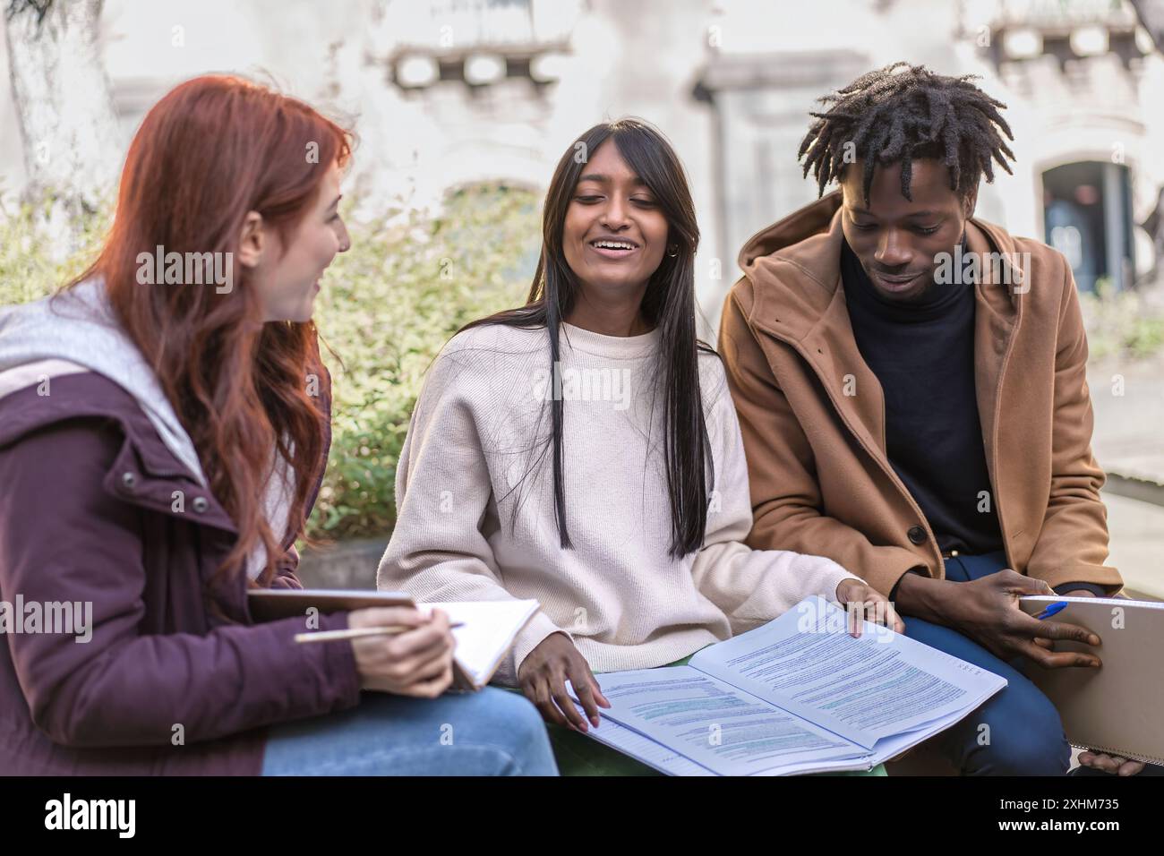 Group of diverse young adults studying together outdoors on university ...