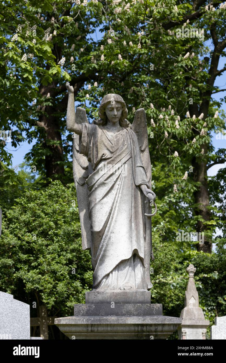 A winged angel statue on a grave, with raised hand as though blessing ...