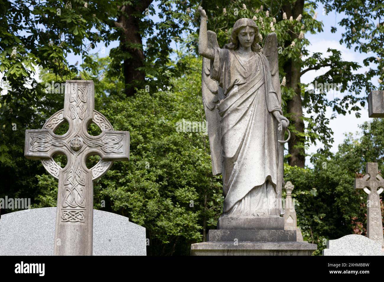 A Celtic cross beside a stone statue of a angel with background of ...
