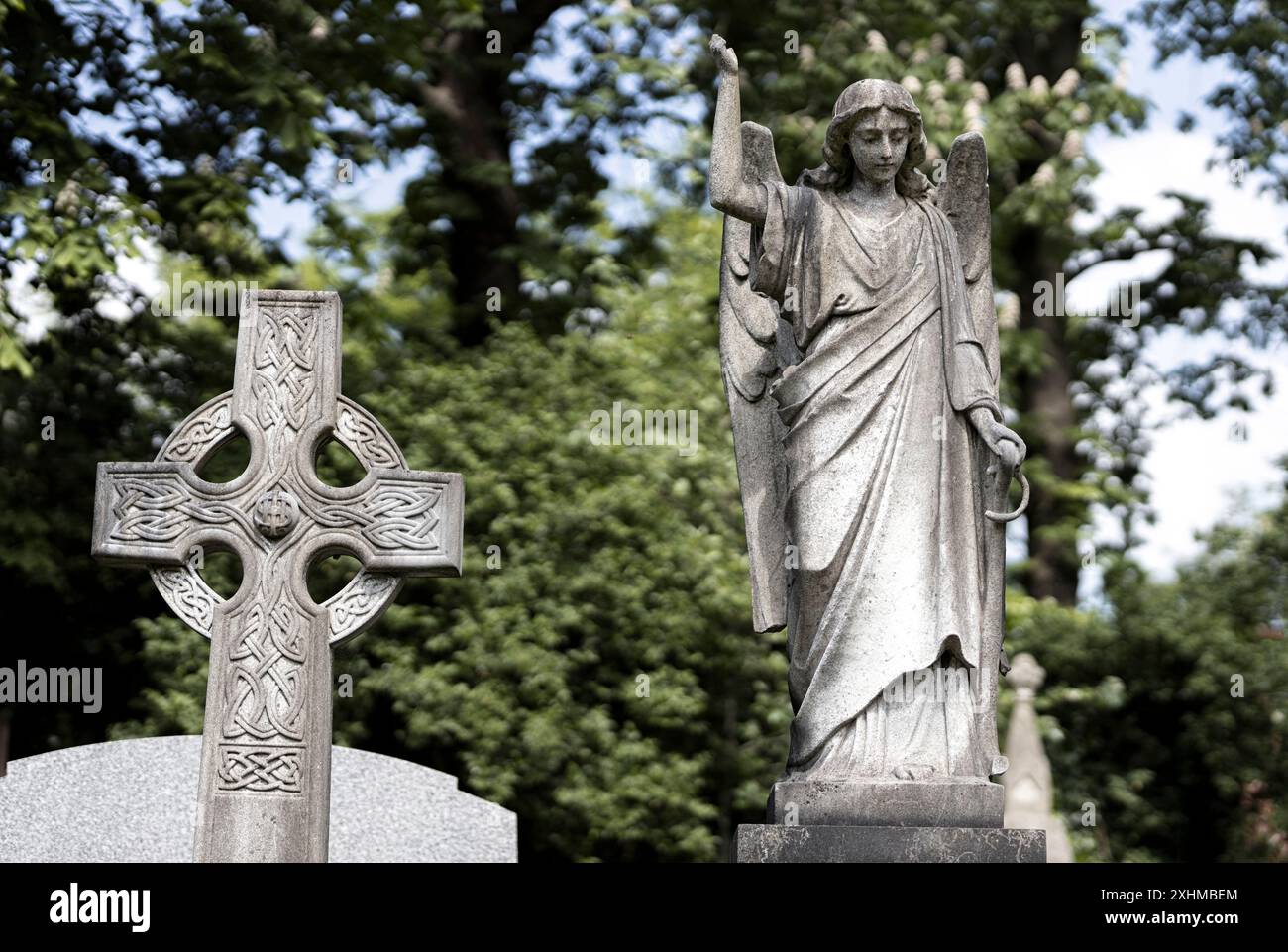 A Celtic cross beside a stone statue of a angel with background of ...