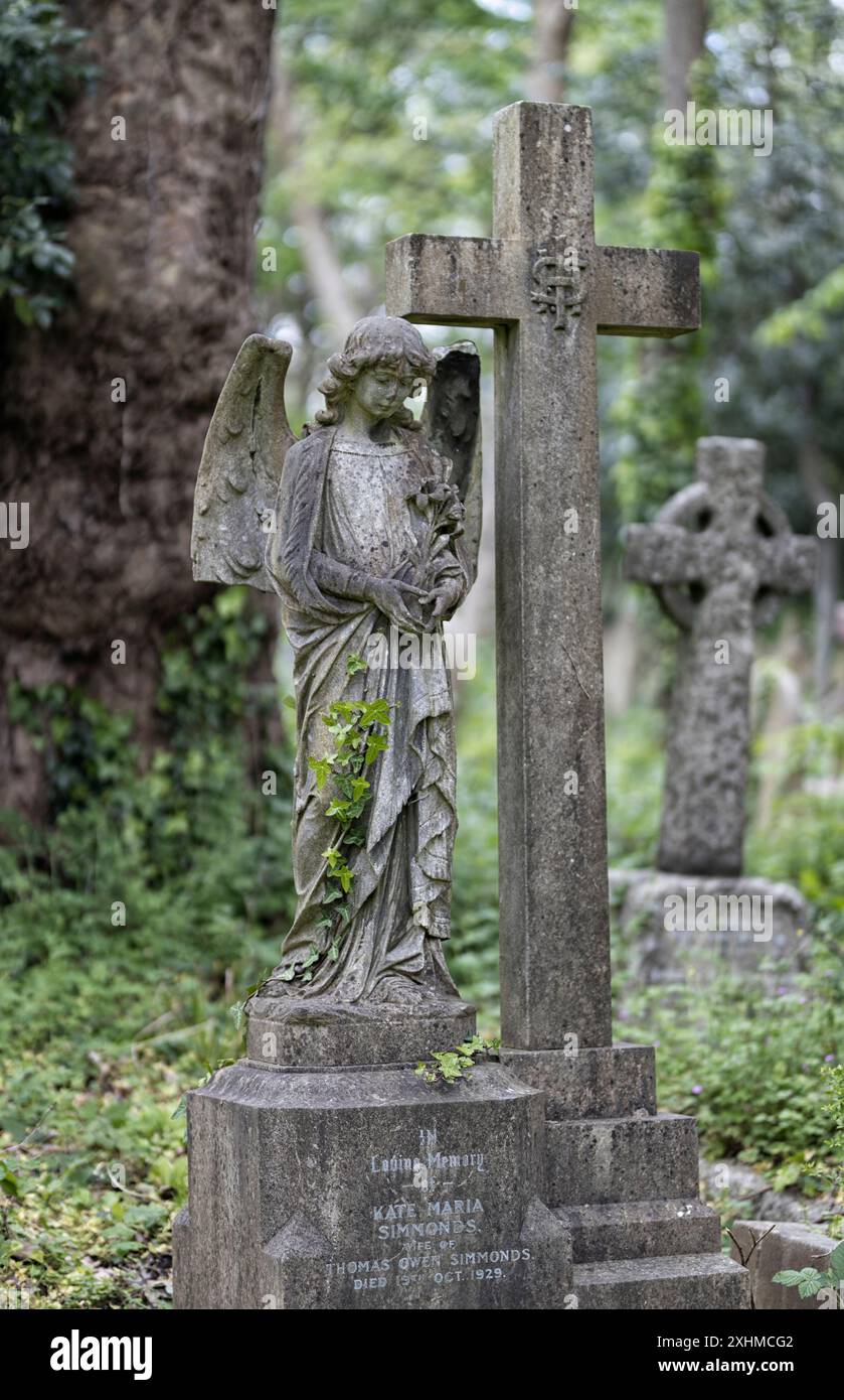 An old angel or cherub statue with a cross beside it in Highgate ...