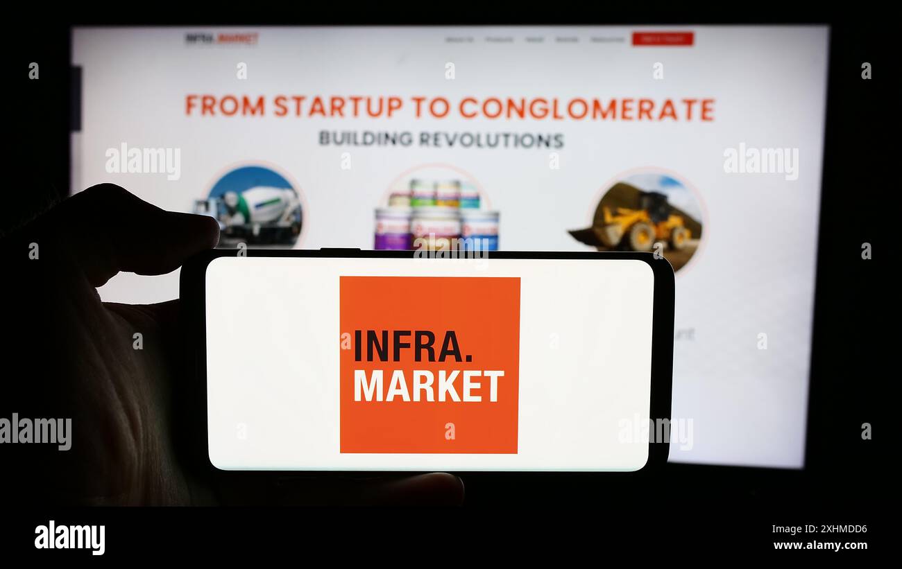 Person holding cellphone with logo of Indian company Hella Infra Market ...