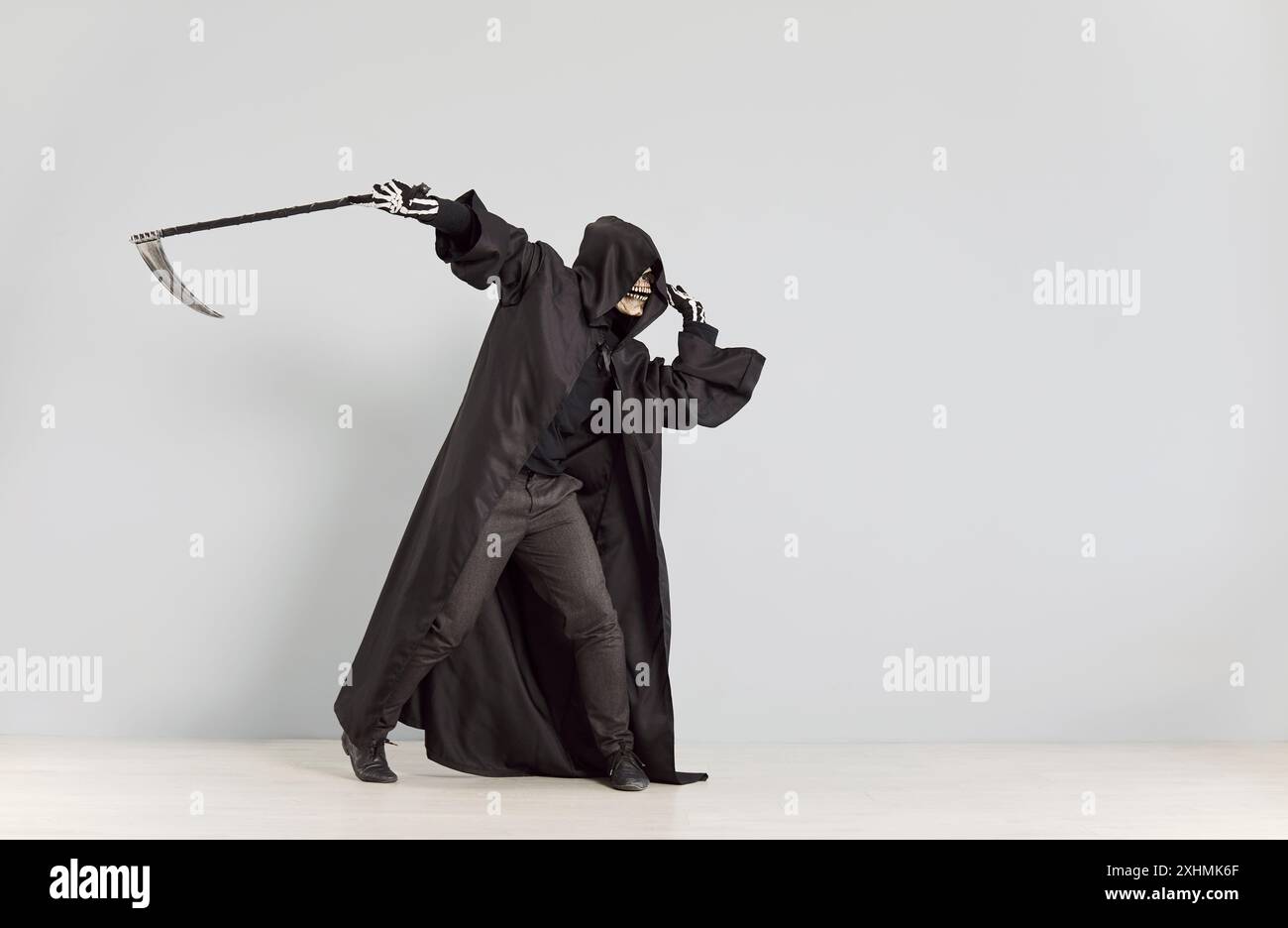 Man in grim reaper death costume swings scythe, having fun on Halloween ...