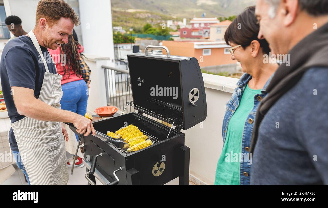 Happy friends cooking corn at barbecue rooftop dinner ...