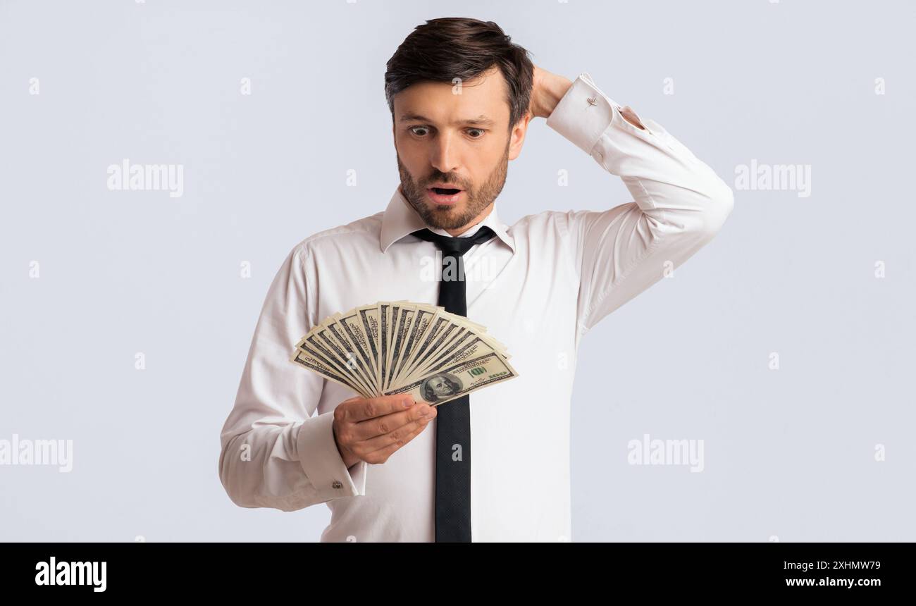 Shocked man holding money scratching his head, studio shot Stock Photo ...