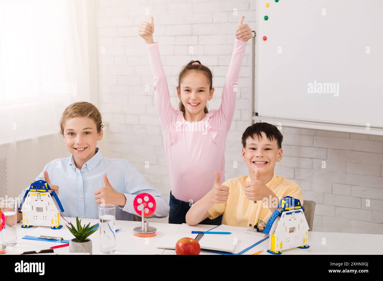 Three Smiling Students Giving Thumbs Up In A Classroom Setting Stock ...