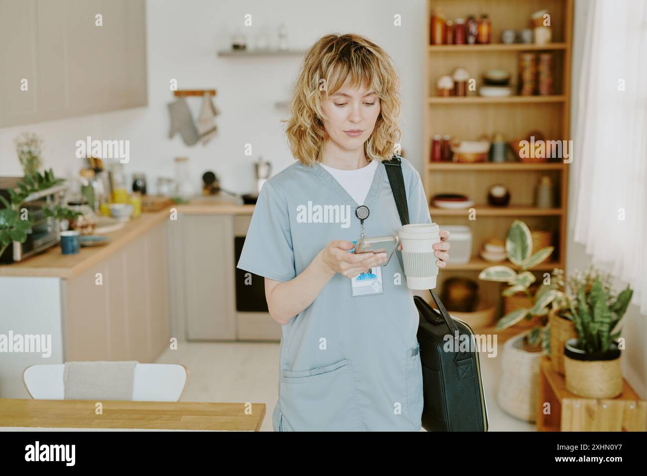 Good looking Caucasian nurse standing in kitchen at home while ...