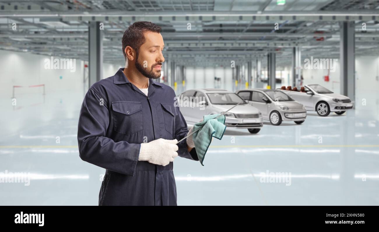 Auto mechanic with parked vehicles cleaning a dipstick for engine oil ...