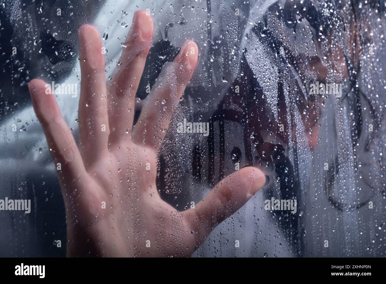 Portrait of Man wearing raincoat behind wet glass. Touching the glass ...