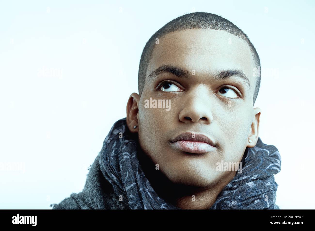 Man in a grey coat and blue patterned scarf, touching his chin ...