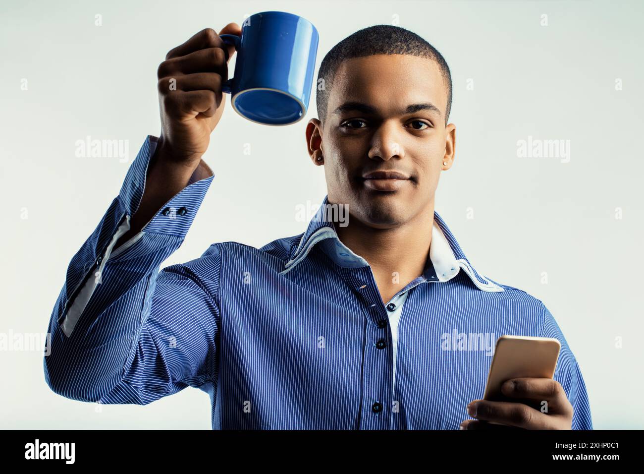 Calm young man, holding a blue coffee mug and a smartphone. His blue ...