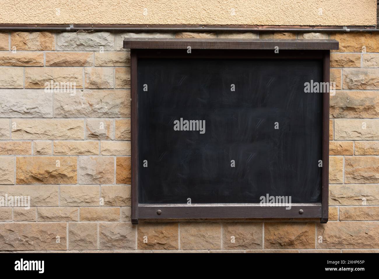 A black inscription board hangs on a stone wall. Black board on an old ...
