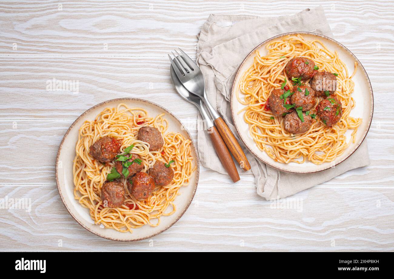 Two plates of delicious spaghetti with meatballs served on white wooden ...
