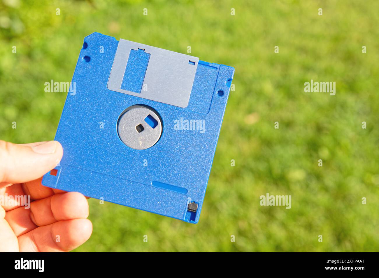 Vintage colored floppy disk in a hand on green grass lawn background ...