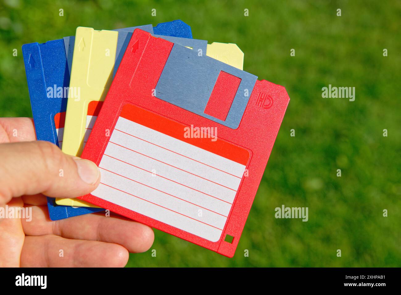 Vintage colored floppy disks in a hand on green grass lawn background ...