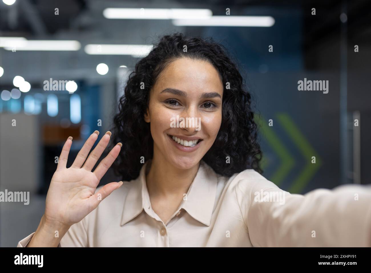 Smiling woman in office waving at camera during video call. Friendly ...