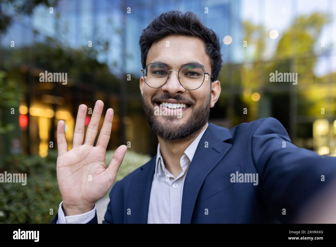 Hispanic businessman wearing glasses and suit smiling and waving at ...