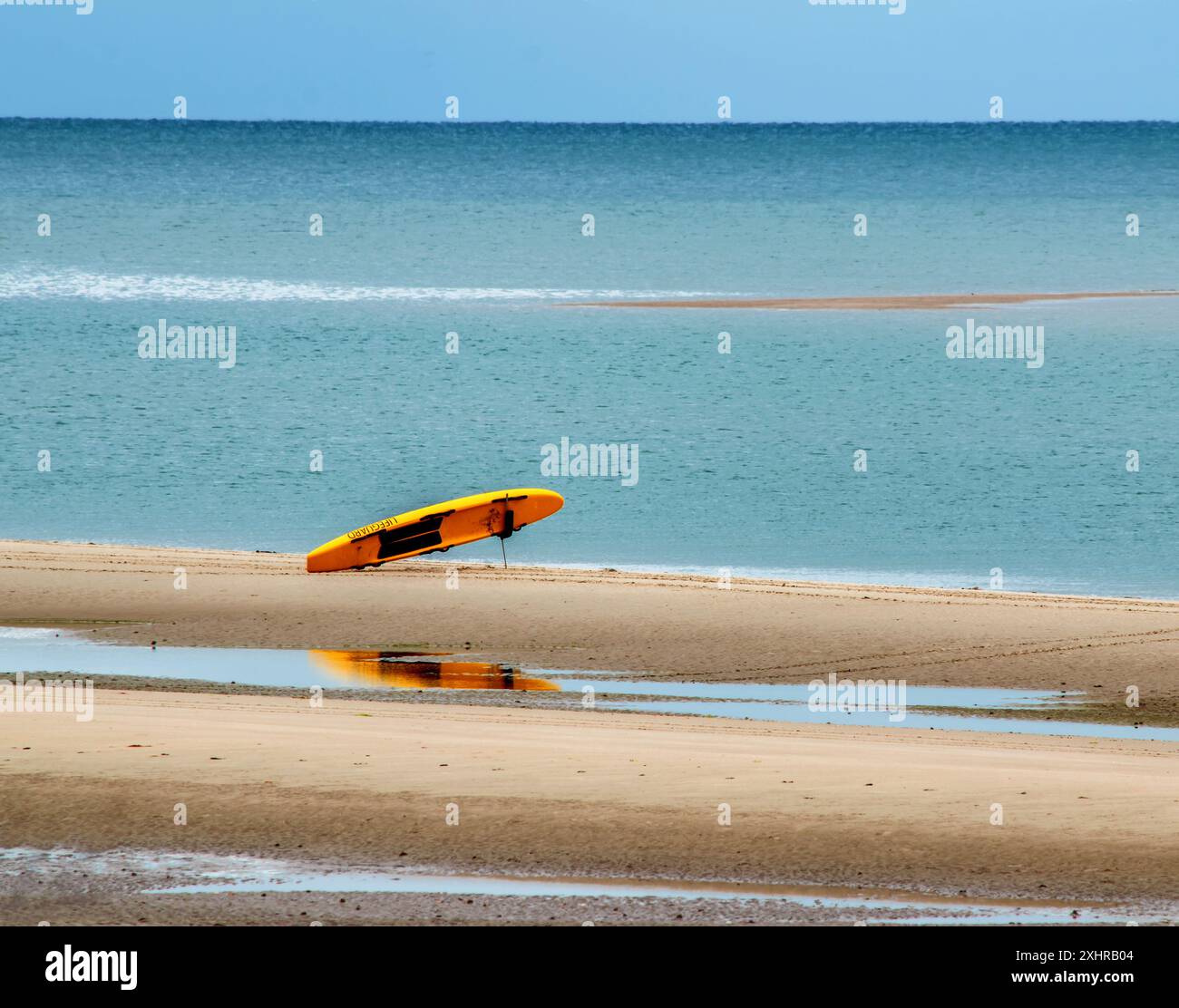 A bright yellow rescue boat is propped up and reflected on the beach ...
