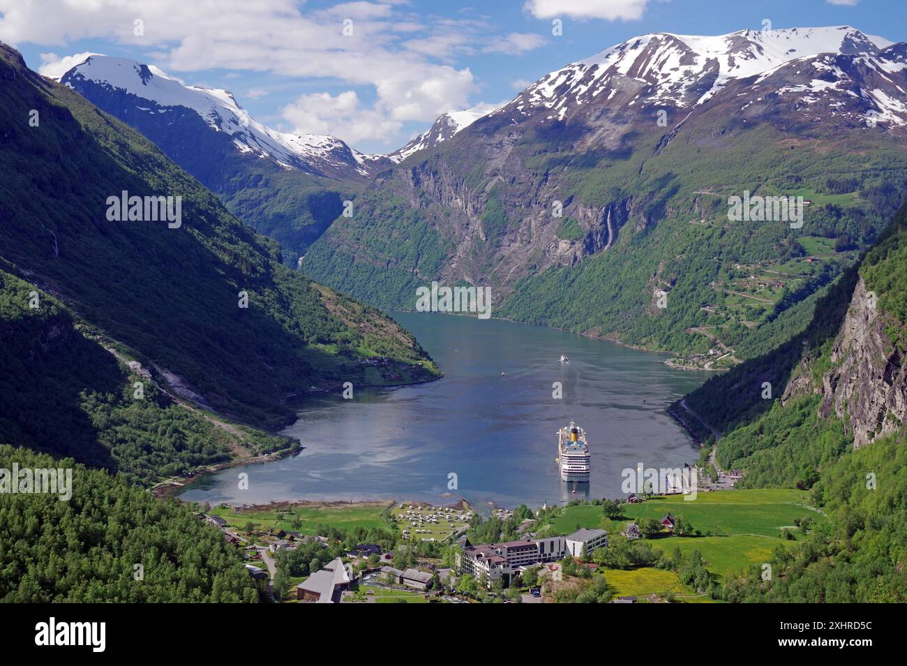 A fjord with a cruise ship surrounded by green mountains with snow ...