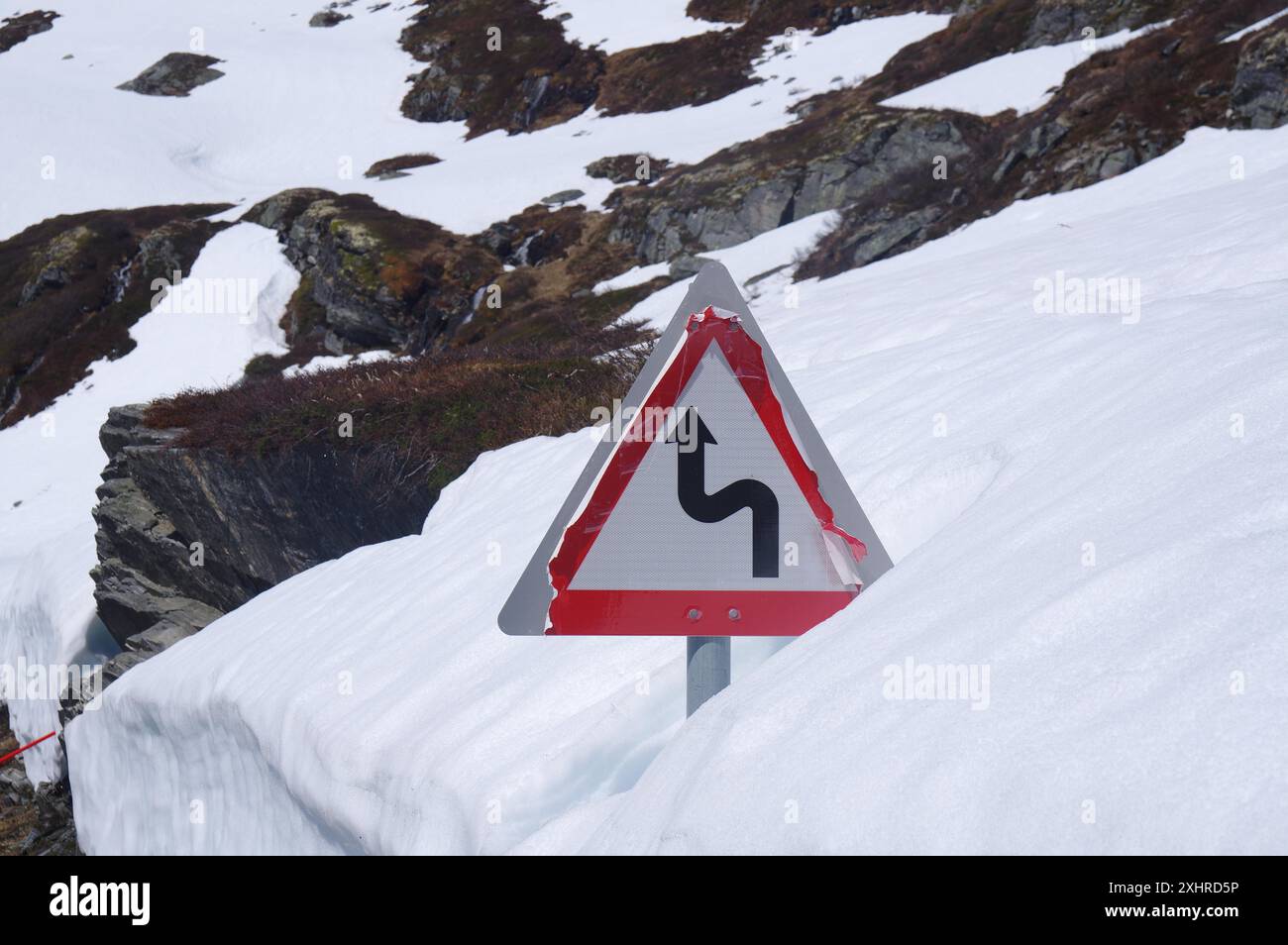 Traffic sign on a snow-covered mountain road indicating a sharp bend ...