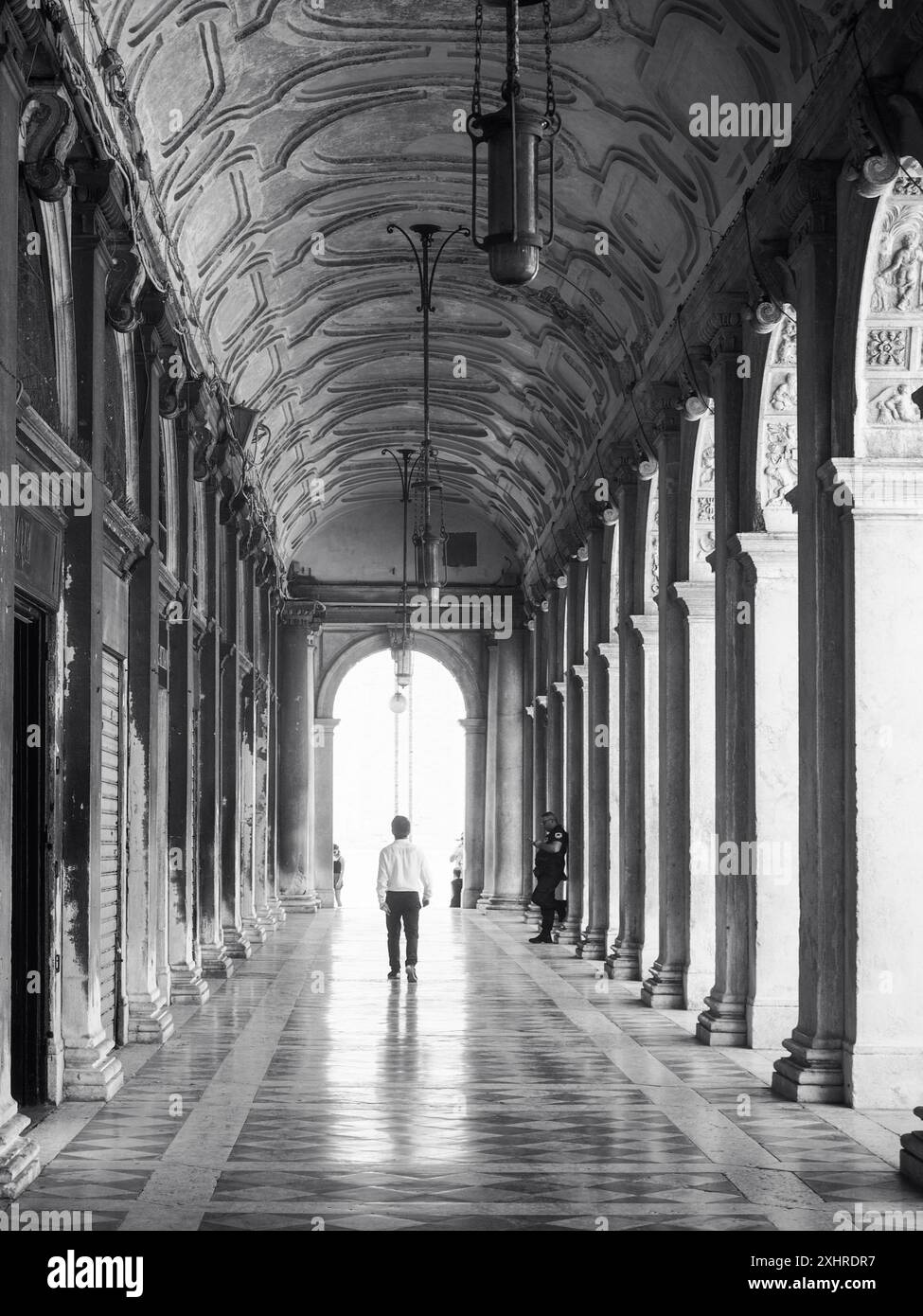Long colonnade with arches and columns, a single person walking through ...