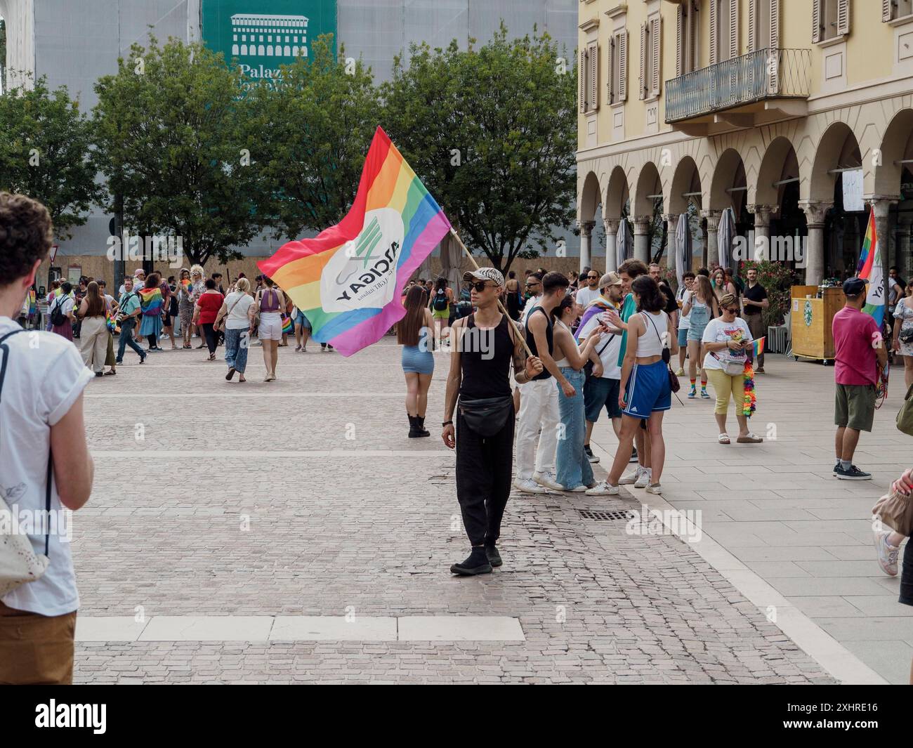 Person holding a pride flag in a crowded square during an outdoor event ...