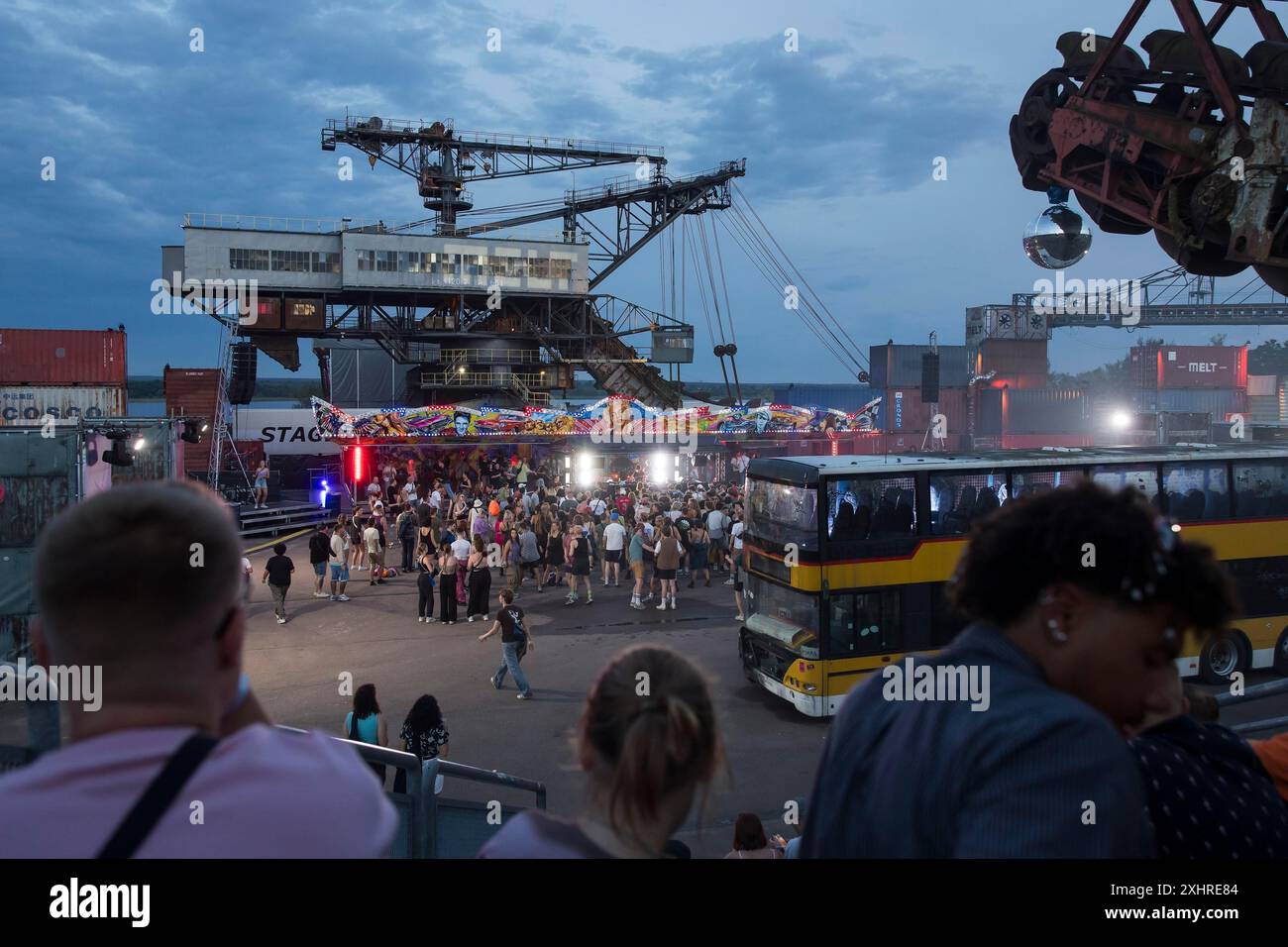 Festival visitors dance in front of a bumper car and between excavators ...