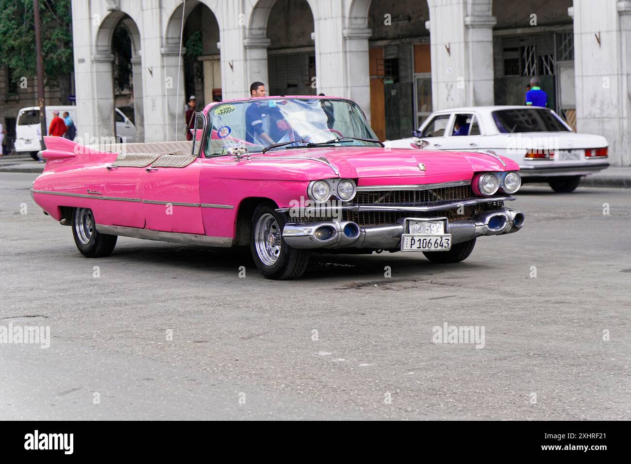 A pink-coloured retro convertible drives on a road in front of ...