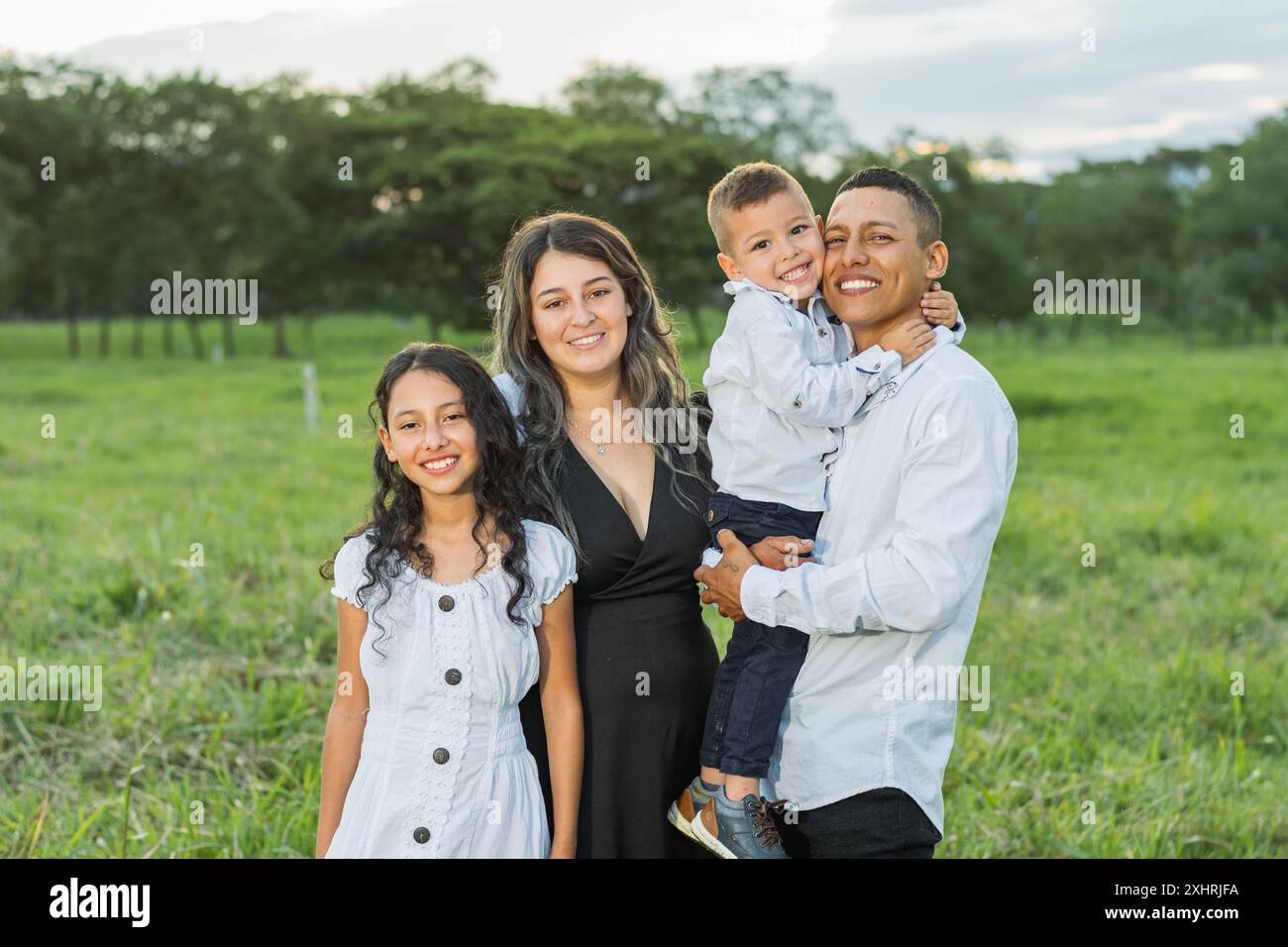 latin family posing happily in a green field, all four are smiling ...