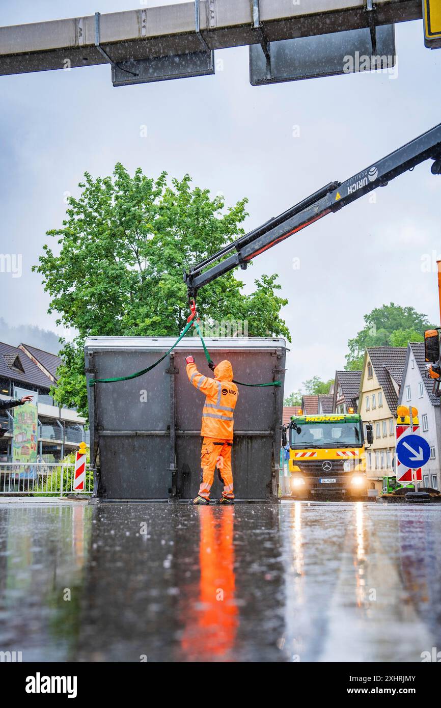 A worker in orange rain gear operates a lifting crane in a rainy street ...