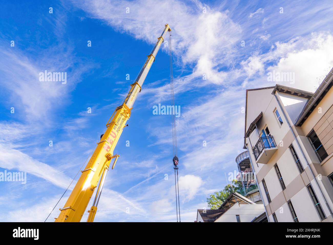 A yellow lifting crane rising into the blue sky with buildings in the ...