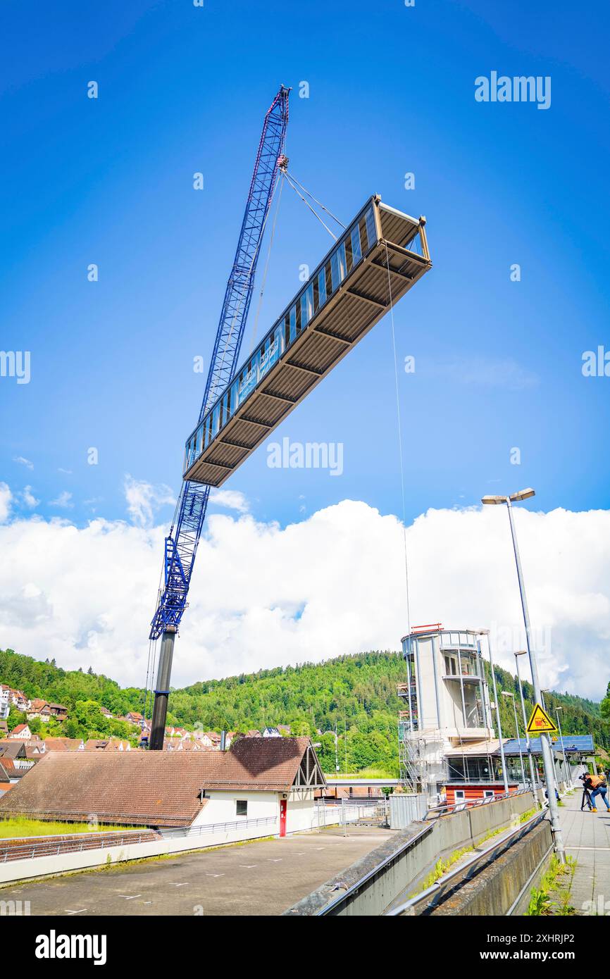 A crane lifts a bridge over a building complex in sunny weather with ...