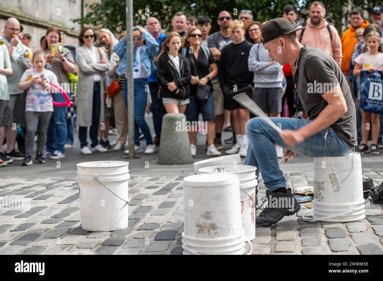 Street musician surrounded by spectators drumming on empty buckets ...