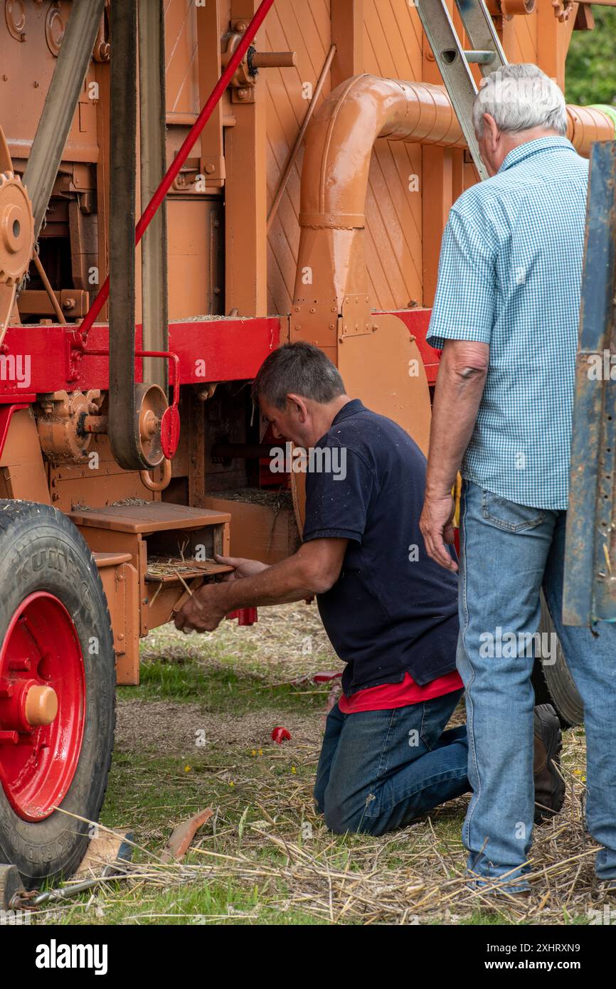 two older men working on a farming implement at a vintage tractor show ...