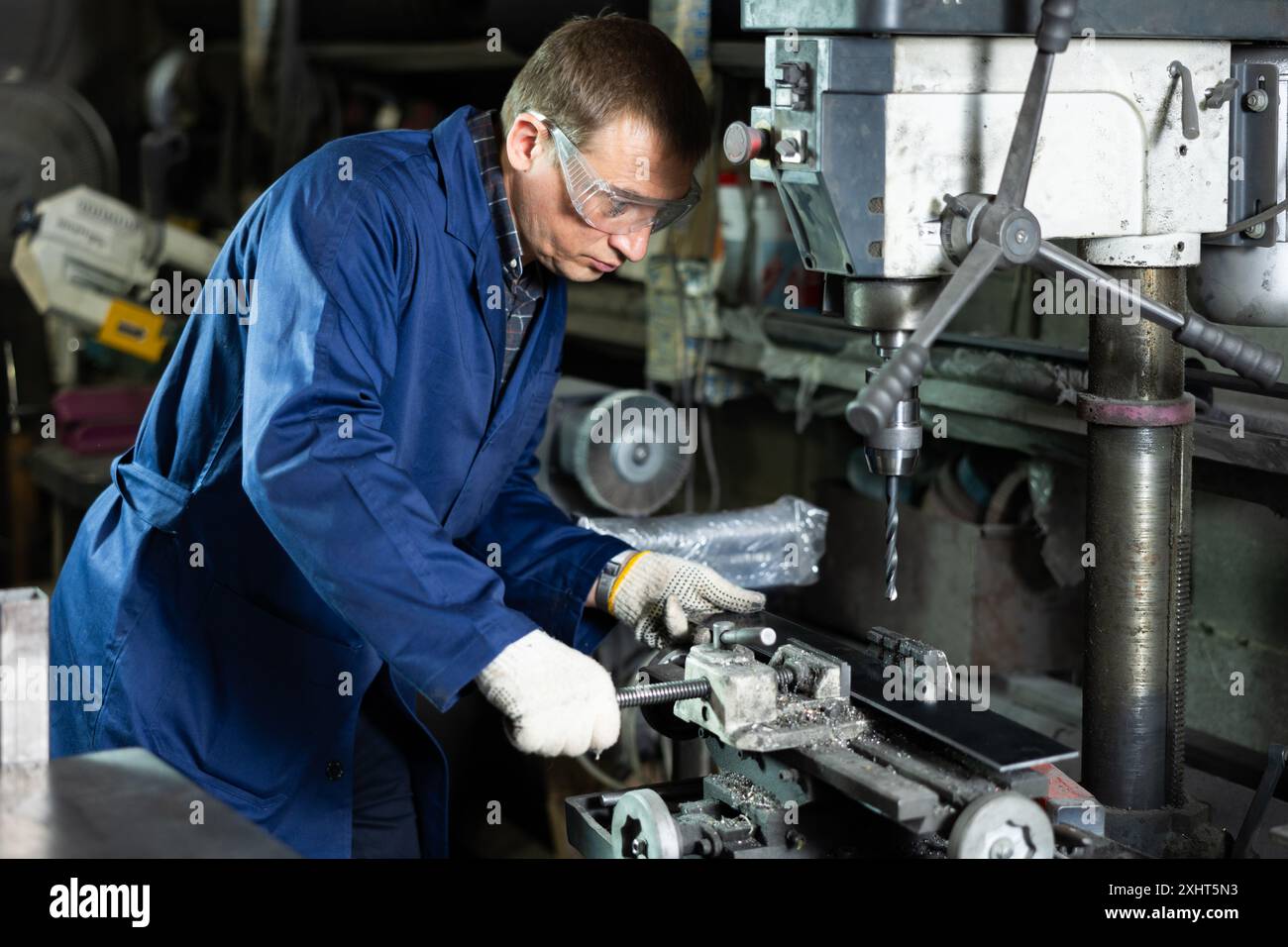 Experienced machinist using drill press in industrial metal workshop ...