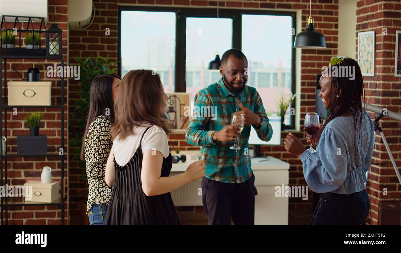 BIPOC group of young adults dancing at apartment party while drinking ...