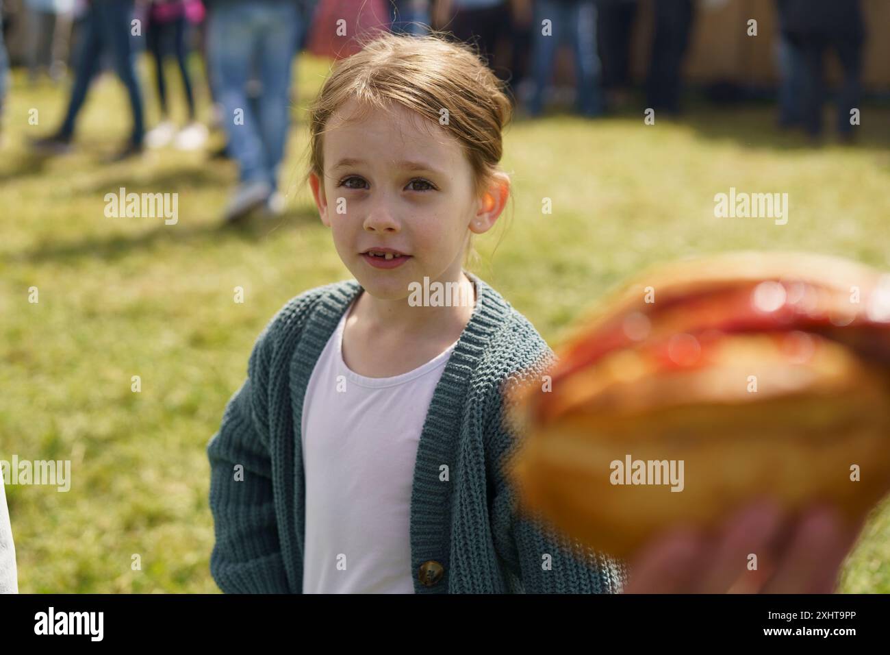 A little toothless girl looks with desire at her sister's hot dog on an ...