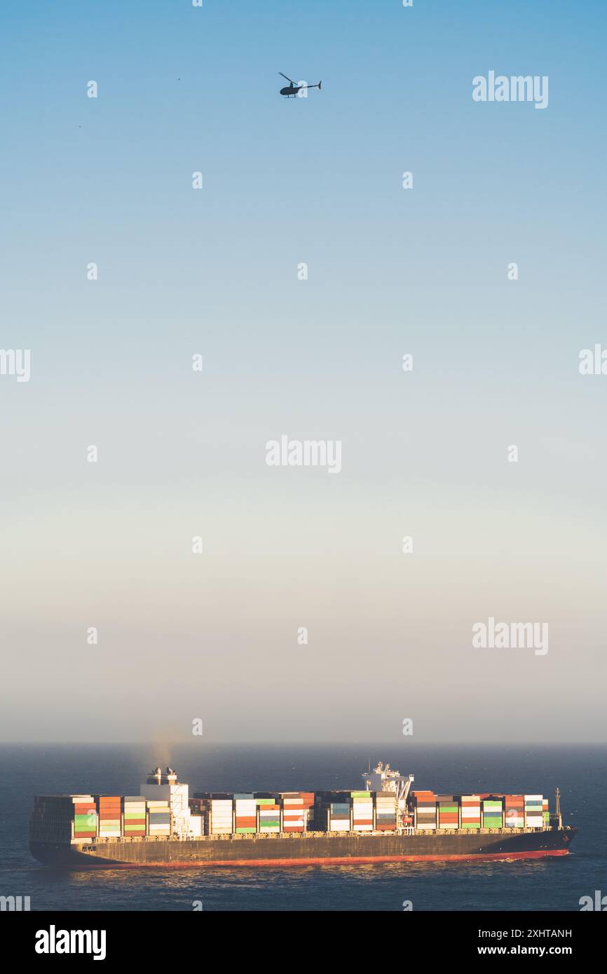 A cargo ship loaded with colorful shipping containers sails on the ...