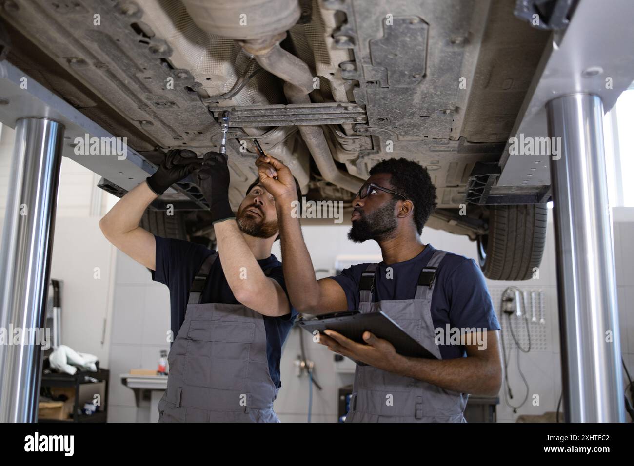 Mechanics working under car on lift in auto repair shop Stock Photo - Alamy