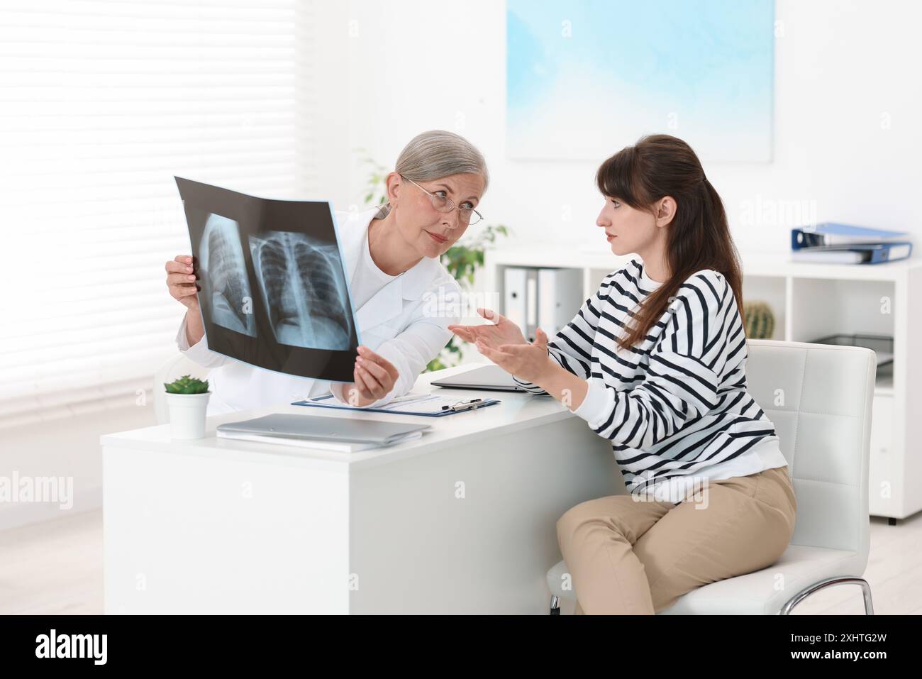 Lung disease. Doctor showing chest x-ray to her patient at table in ...
