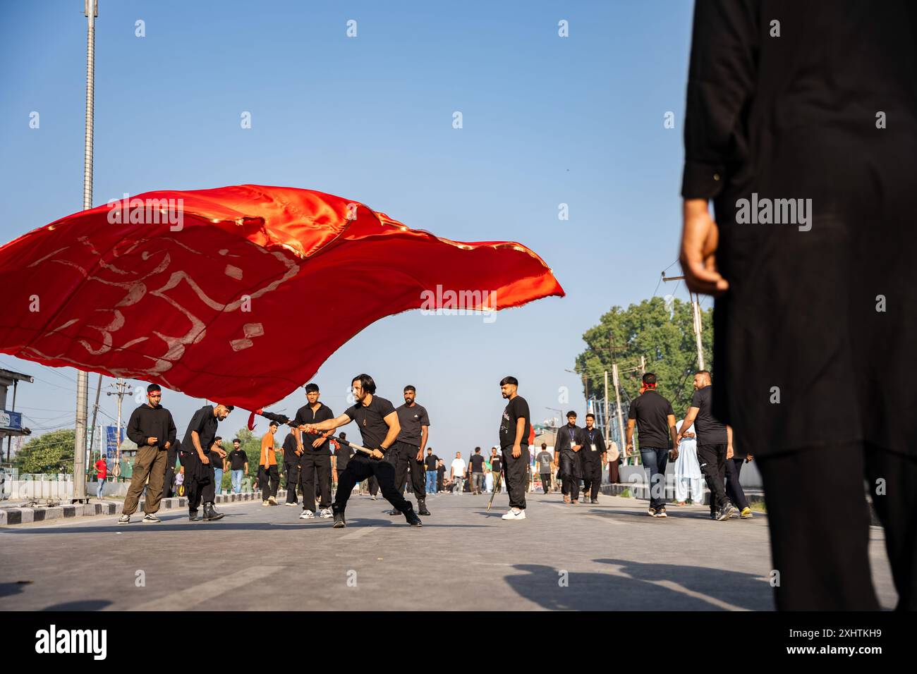 A Kashmiri Shia Muslim man waves a large religious flag inscribed with "Labaik ya Hussain ...