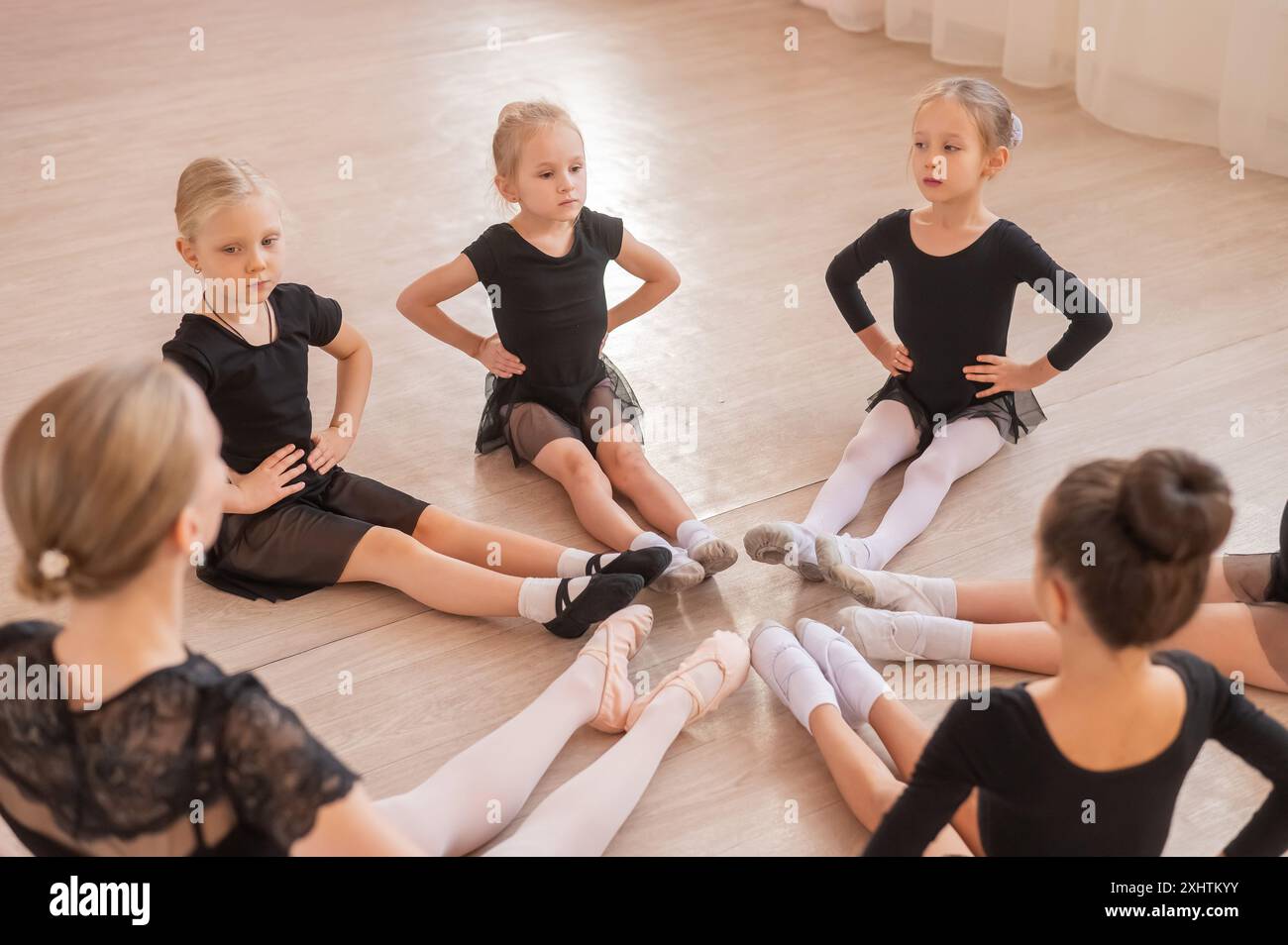 Caucasian woman and five little girls sit in a circle and do stretching ...