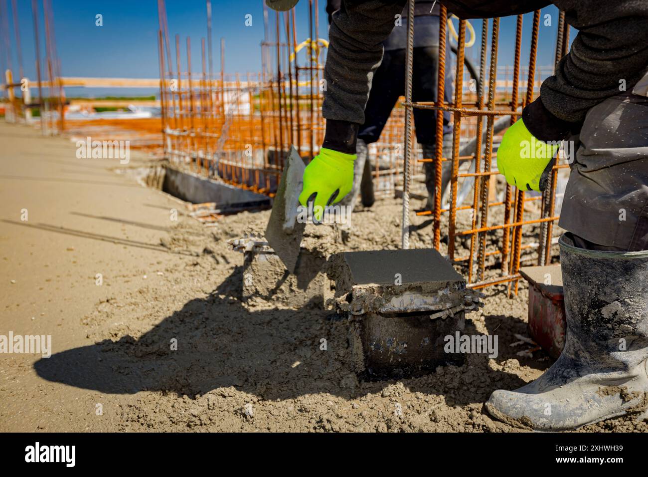 Worker is using trowel to fill up cube mold, full with concrete, sample ...
