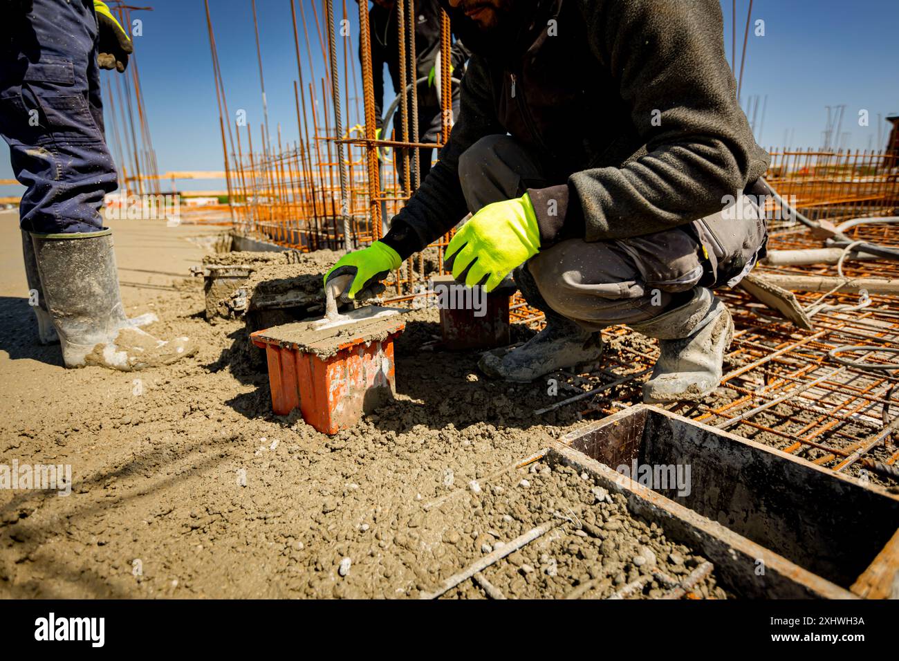 Worker is using trowel to fill up cube mold, full with concrete, sample ...