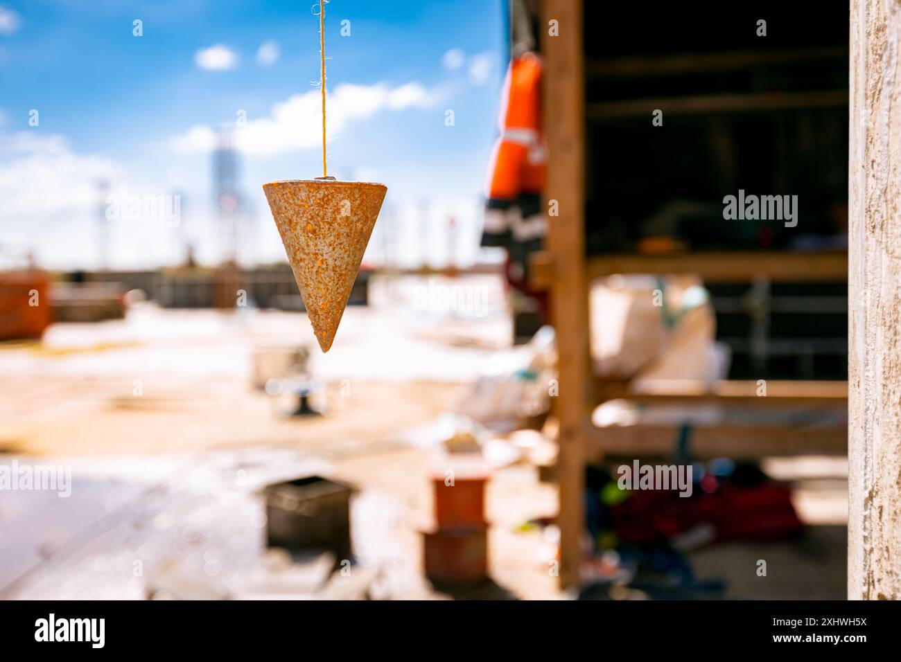 Vertical rusty metal plumb, plummet or plum bob, at building site is ...
