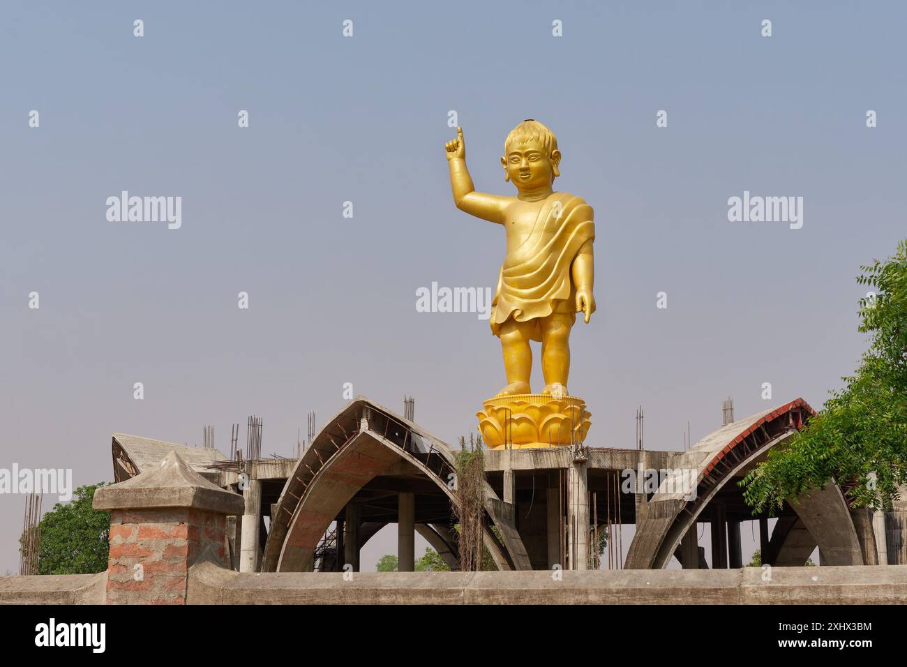 A large golden statue of a child Buddha in front of an unfinished ...
