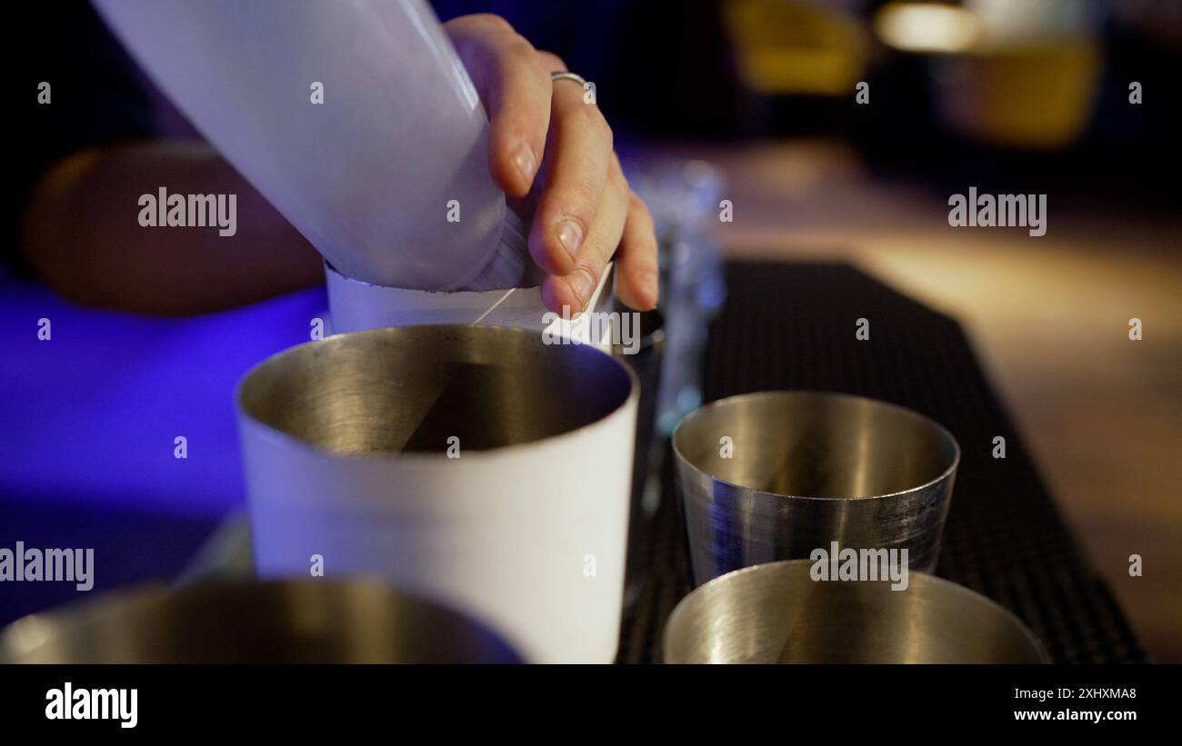 Preparation of alcoholic cocktails. Close-up of a bartender adding ice cubes to a mixing glass ...