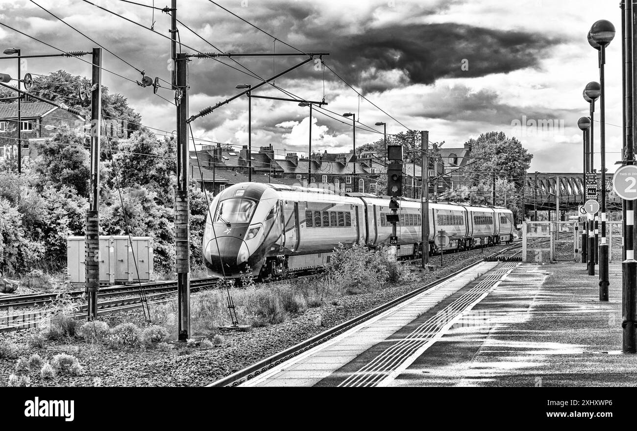 A train with a line of carriages departs a railway station on rainy day ...