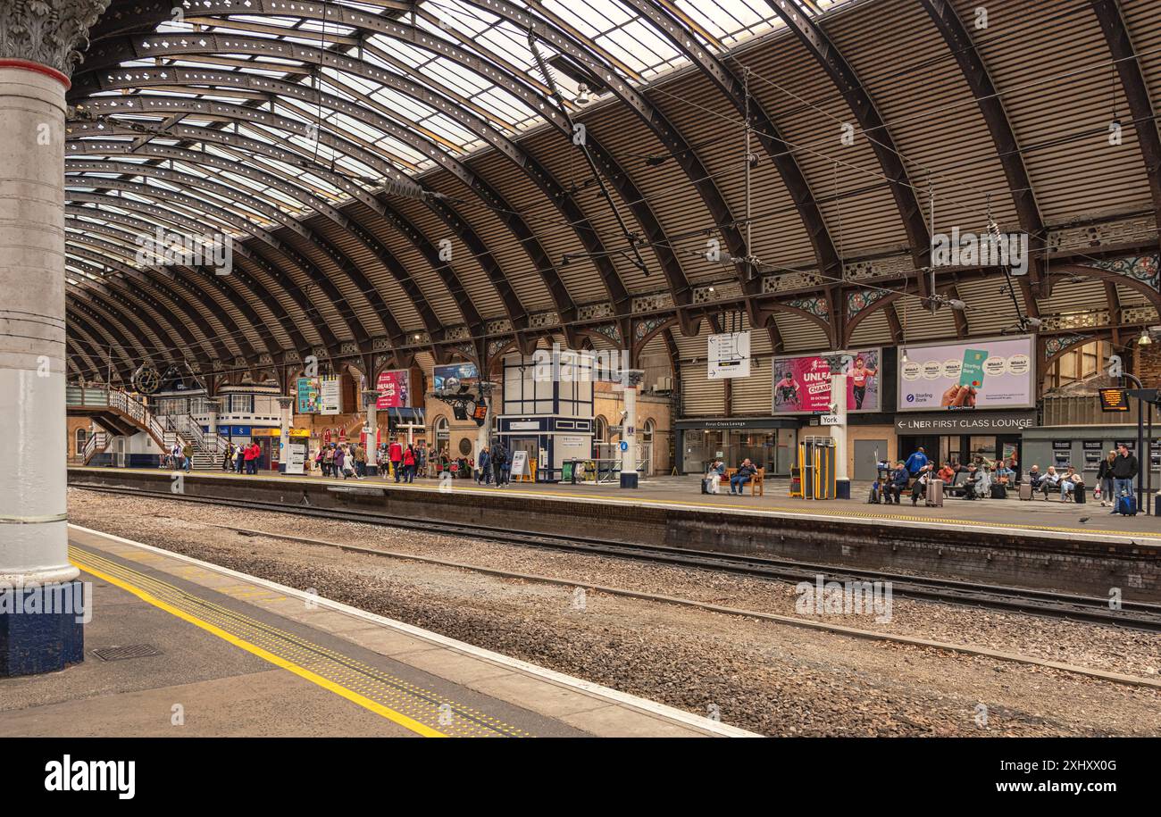 A railway station concourse with passengers waiting for trains. Columns ...