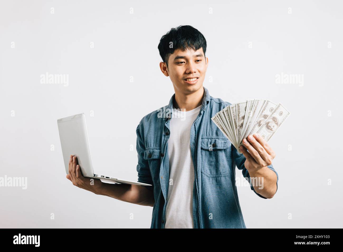Portrait Asian smiling young man holding laptop computer and fan of money cash studio shot ...